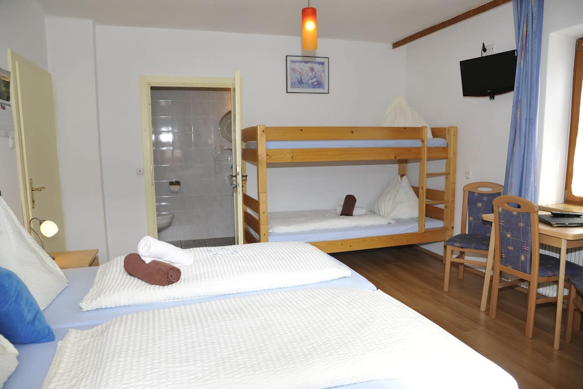 Quarto com beliches, uma escrivaninha com cadeira, televisão e porta.