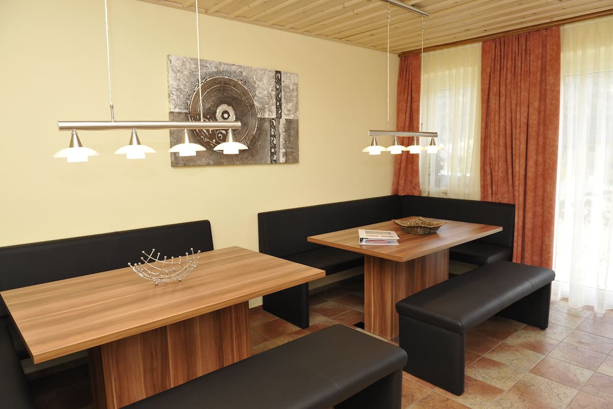 Uma sala de jantar moderna com mesas de madeira e bancos estofados pretos, um lustre pendurado e uma grande obra de arte abstrata na parede.