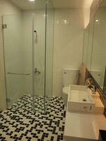 Casa de banho com cabine de duche em vidro, lavatório branco e sanita.