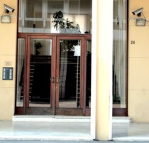 Entrada de um edifício com porta de vidro, planta em vaso e câmera de segurança.