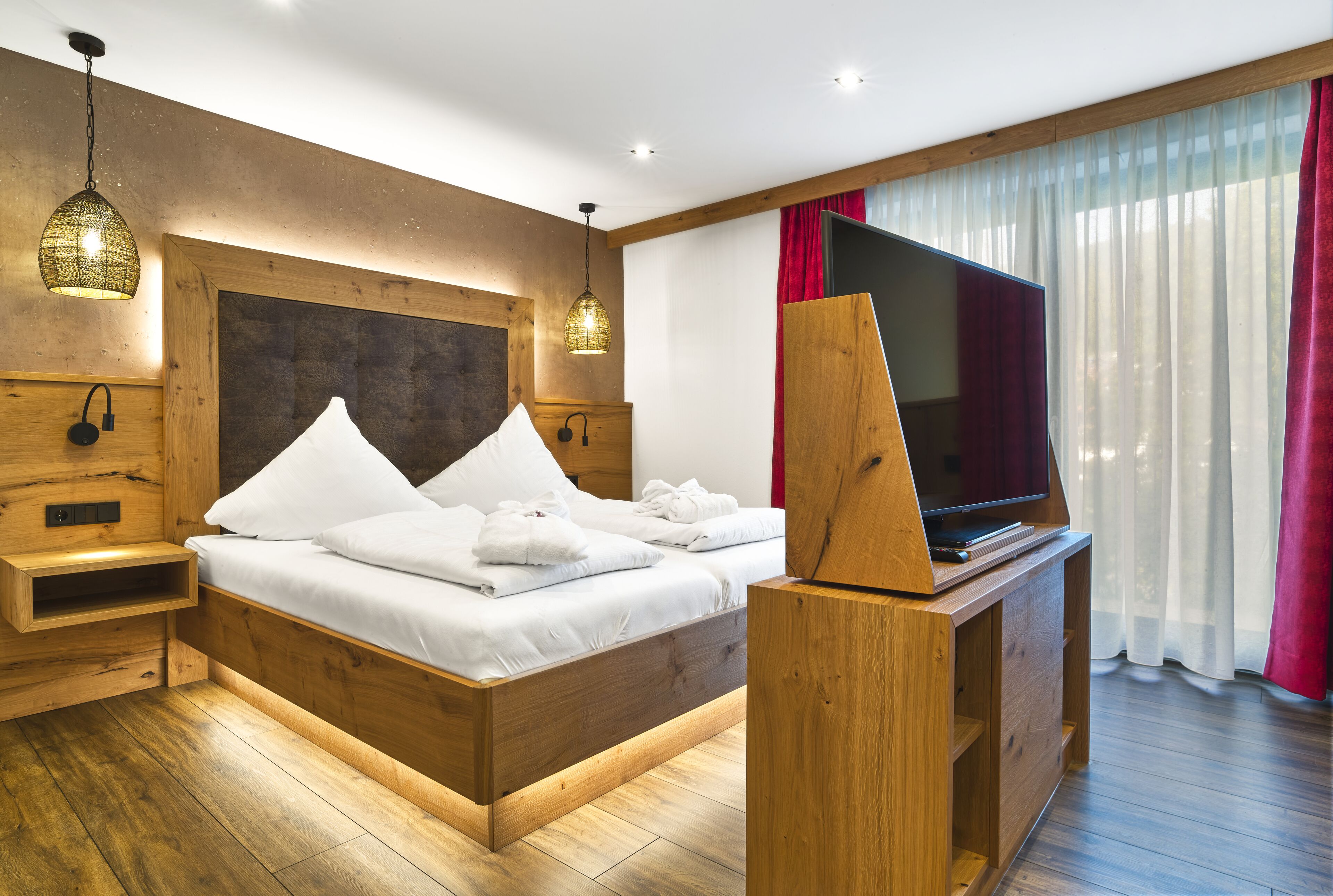Quarto de hotel moderno com cama de madeira, televisão de tela plana e mesa de cabeceira de madeira.