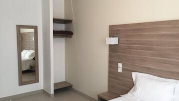 Quarto com cabeceira de madeira, mesa de cabeceira, espelho e guarda-roupa.