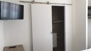 Quarto de hotel com uma cama, uma televisão fixada na parede, uma mesa de cabeceira de madeira e uma porta que dá para o banheiro.