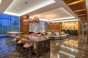 Um hall de hotel moderno com uma receção de mármore, área de estar e grandes janelas.