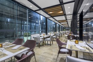 Restaurante moderno com paredes de vidro, várias mesas de jantar e cadeiras de vime.