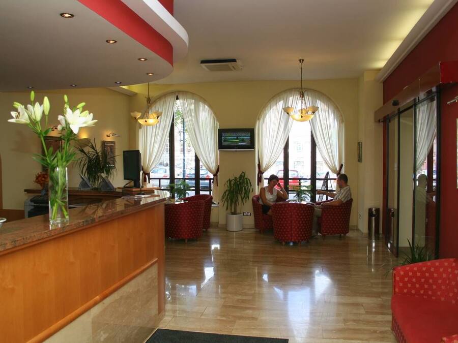 Um saguão de hotel com balcão de recepção, área de estar e grandes janelas com cortinas.