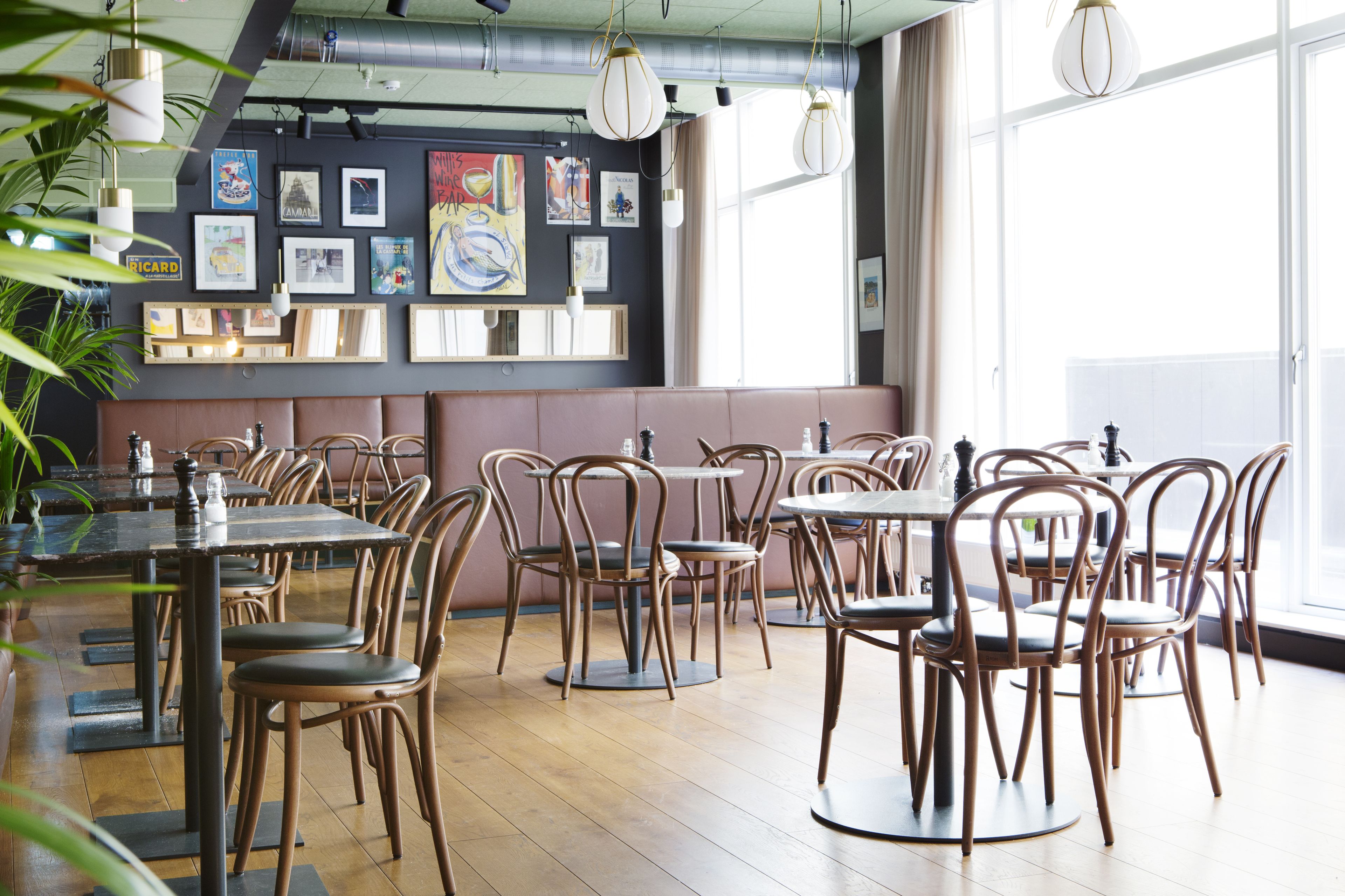Interior de restaurante com mesas e cadeiras de madeira, área de bar e obras de arte nas paredes.
