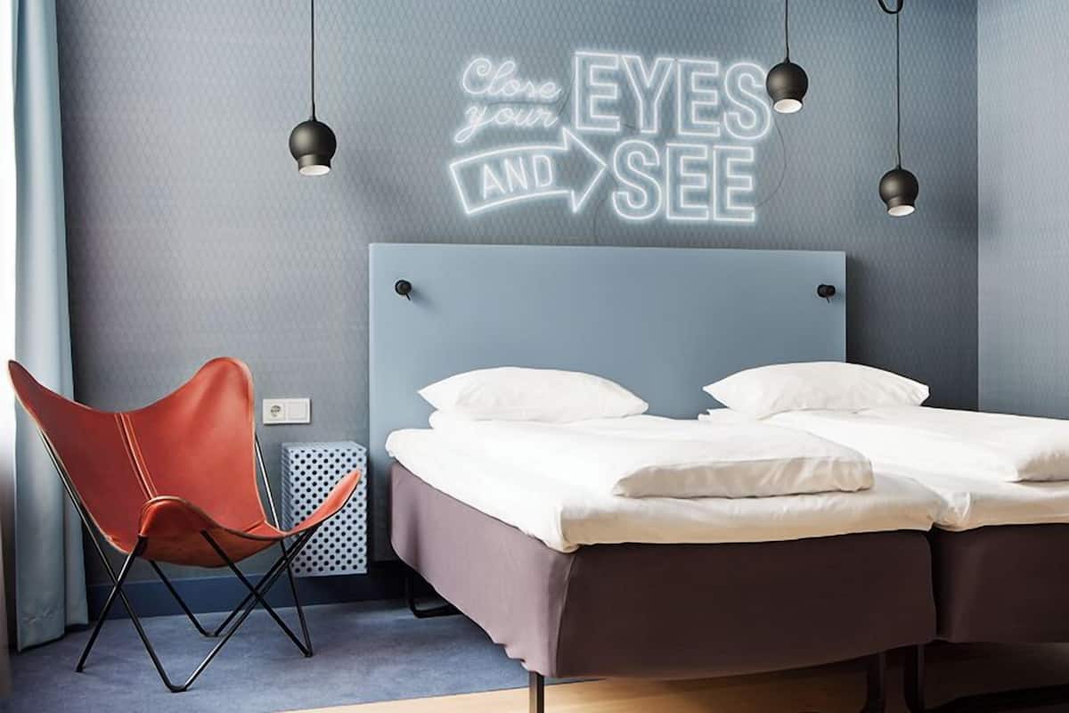 Quarto de hotel moderno com uma cama, uma cadeira vermelha e um letreiro de neon na parede.