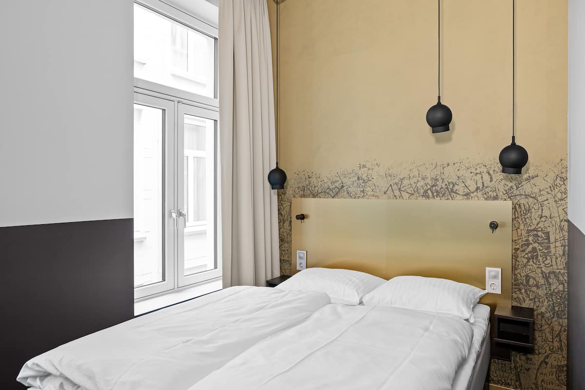 Quarto de hotel com uma cama grande, janela com cortinas e parede com grafite.