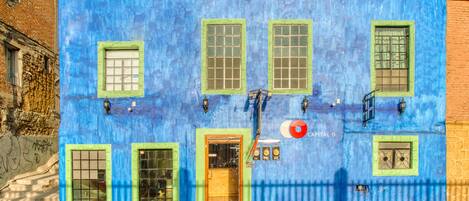 Um edifício de dois andares com fachada azul, molduras de janela verdes e um guarda-sol vermelho no telhado.