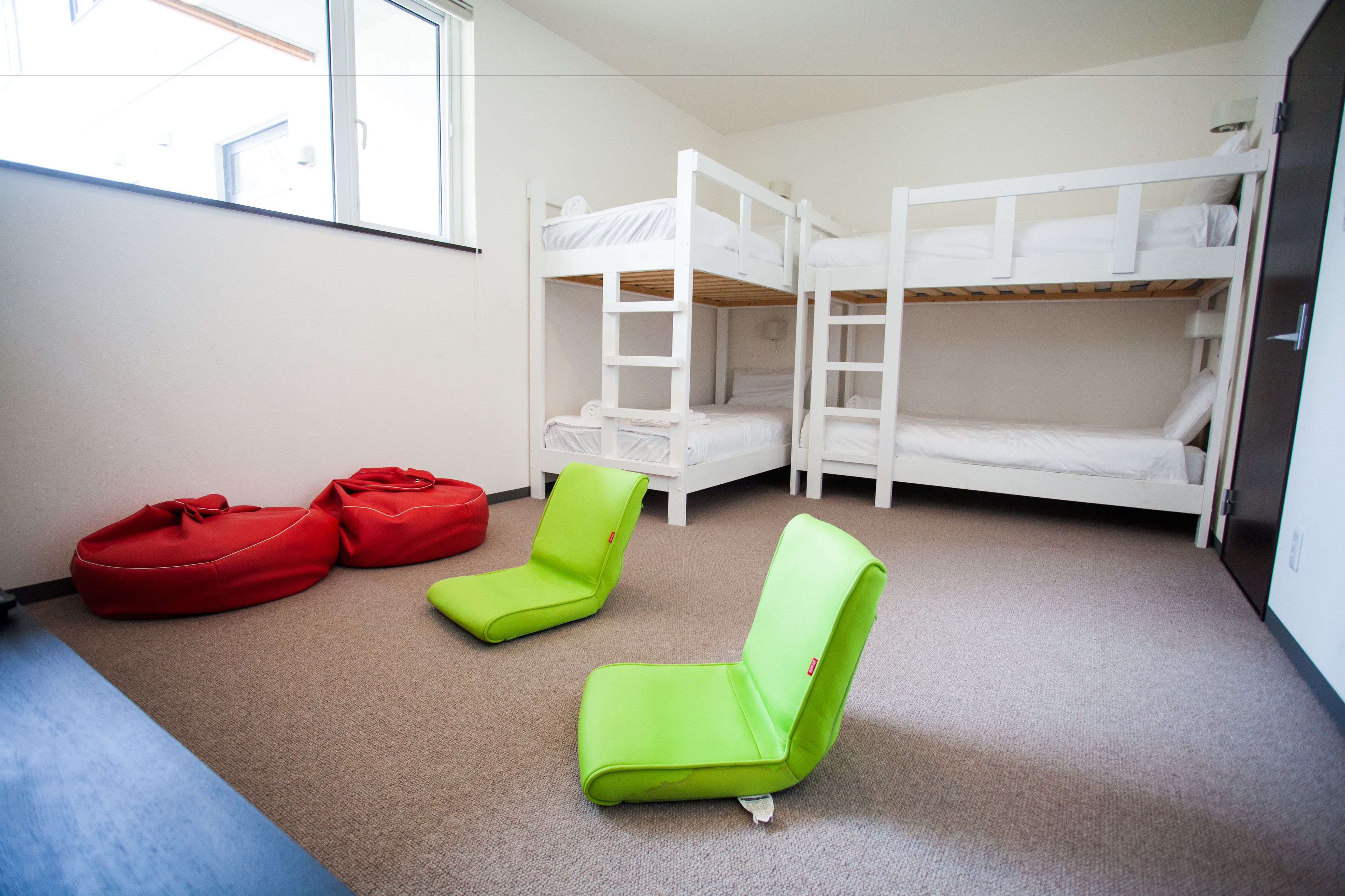 Quarto com beliche, janela, dois sacos de feijão e uma cadeira verde.