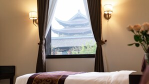 Quarto de hotel com cama, janela com cortinas e vista para arquitetura tradicional.