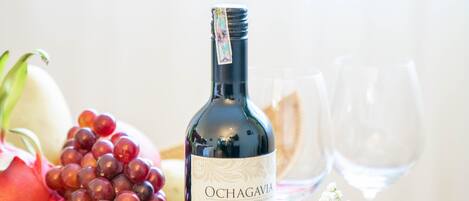 Uma garrafa de vinho Ochagavia Bodega Galicia, uma cesta de uvas, uma melancia e algumas flores sobre uma mesa.