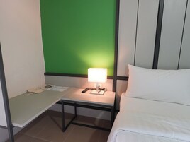 Quarto de hotel com cama, mesa de cabeceira com luminária, uma mesinha e parede verde.