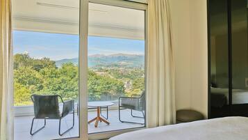 Quarto de hotel com uma grande porta de correr de vidro que dá para uma varanda externa com mesa e cadeiras, uma cama e um guarda-roupa.