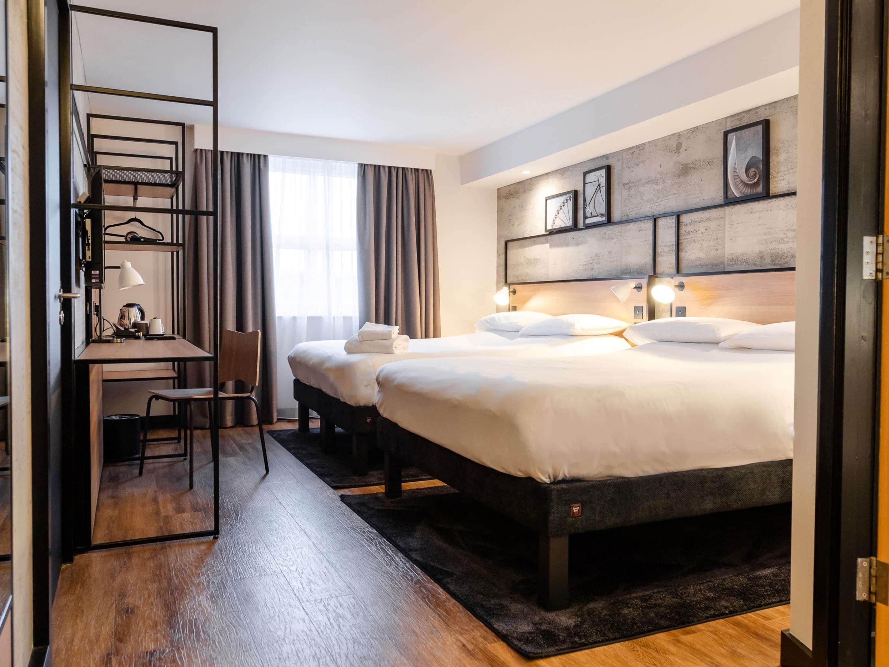 Quarto de hotel com duas camas, uma escrivaninha e uma cadeira.