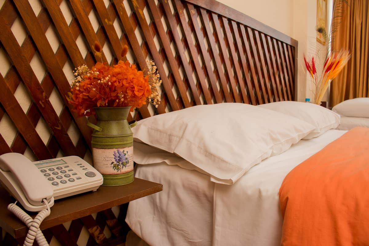 Quarto de hotel com cabeceira de madeira, mesa de cabeceira com telefone e um vaso de flores.