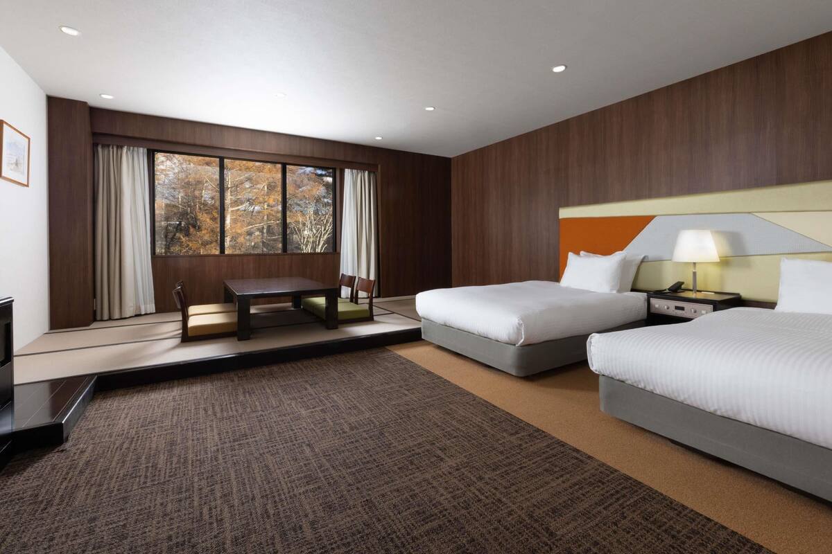 Quarto de hotel com duas camas, uma escrivaninha e janela com cortinas.