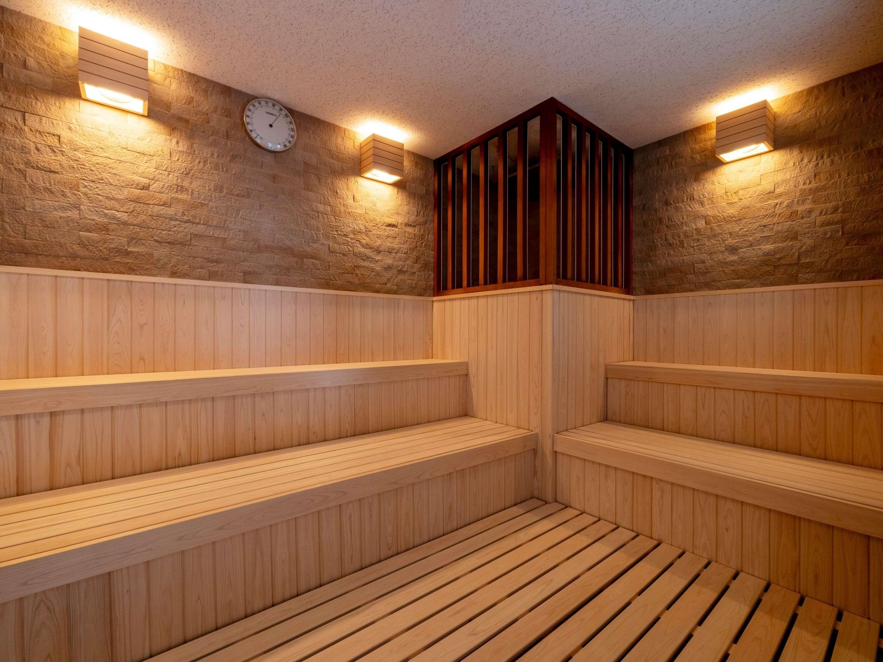 Uma sauna com bancos de madeira, um relógio e luminárias fixadas na parede.
