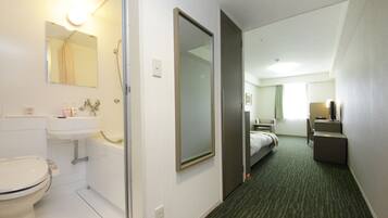 Quarto de hotel com banheiro, cama, escrivaninha e televisão.