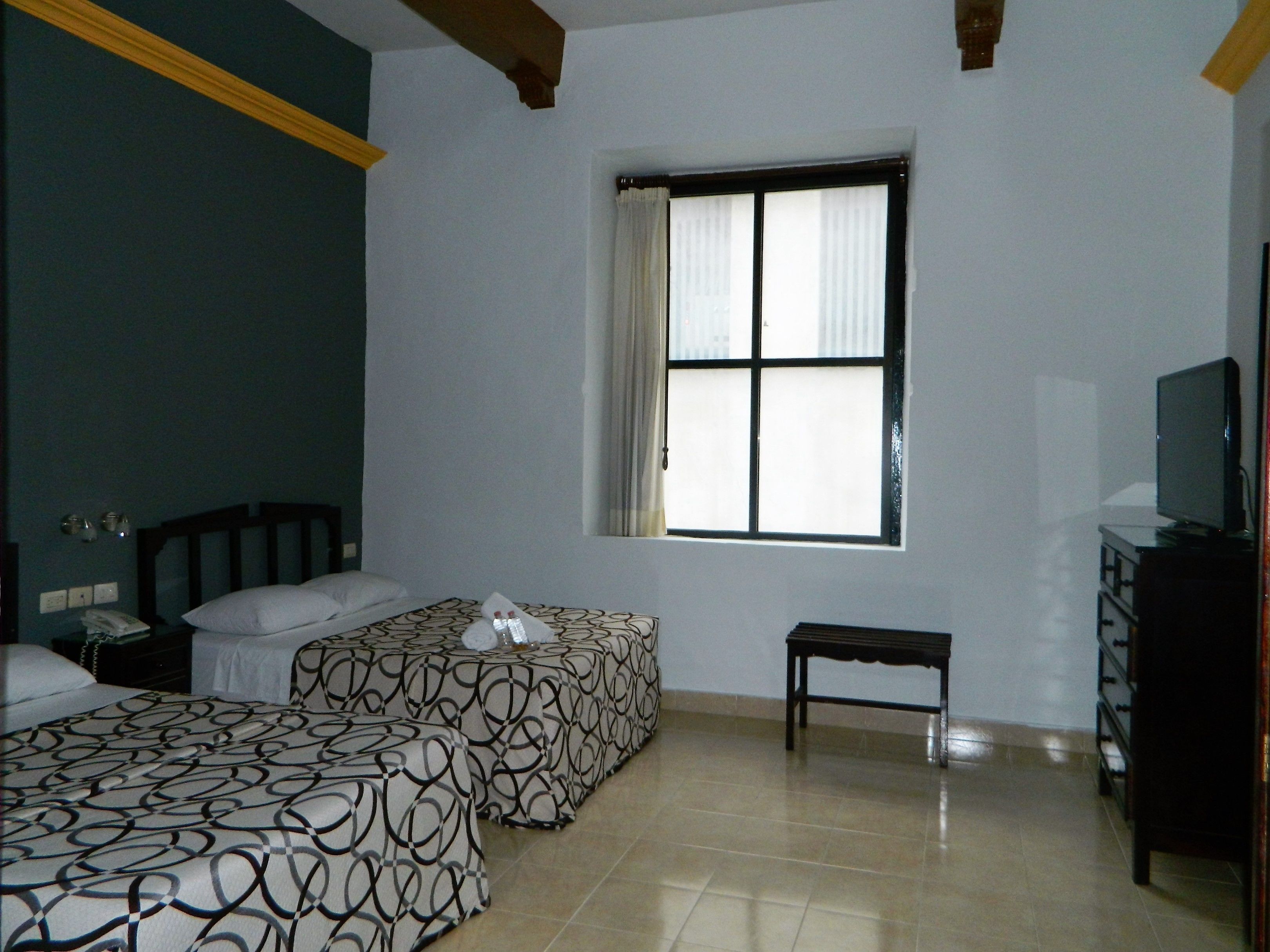 Quarto com duas camas, uma janela, uma televisão e uma mesa pequena.