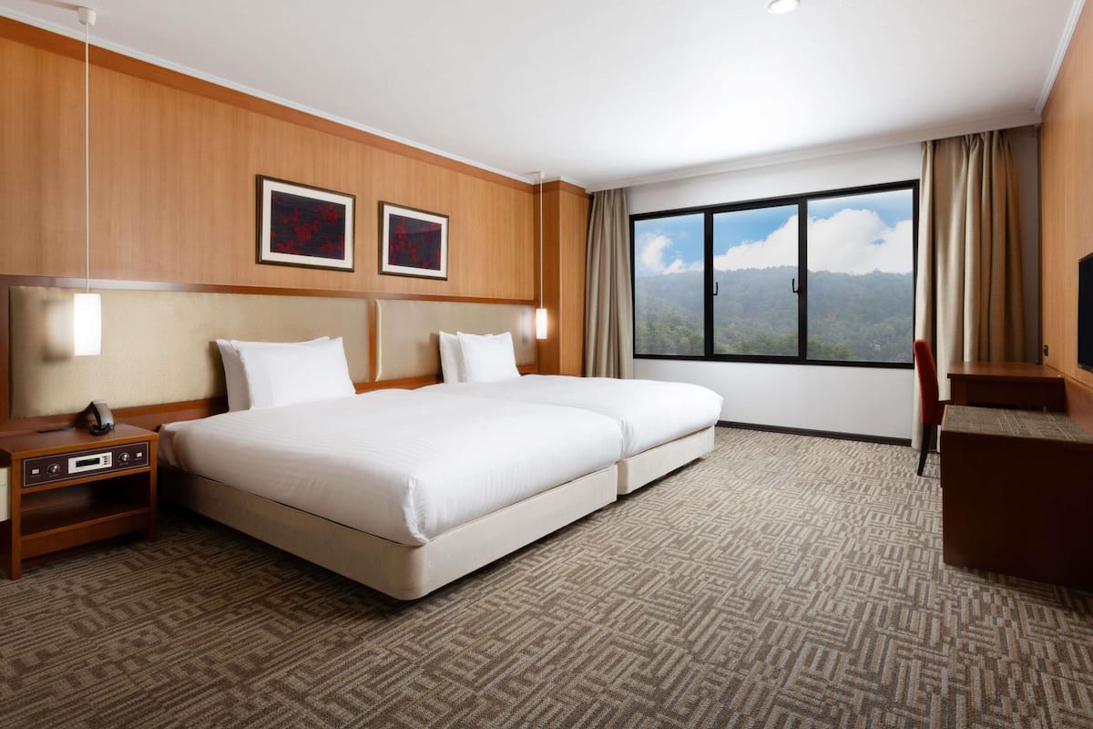 Quarto de hotel com uma cama grande, uma escrivaninha, uma cadeira, uma mesa de cabeceira e uma janela com vista para as montanhas.