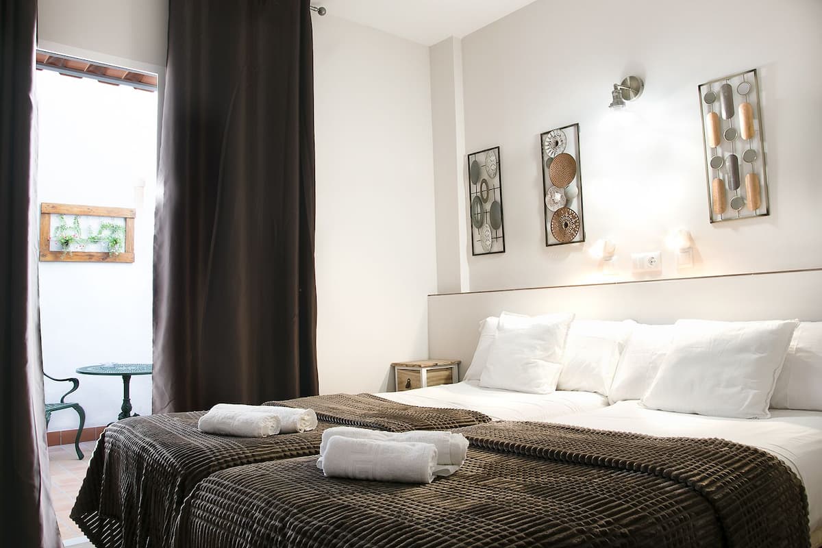 Quarto de hotel com uma cama grande, duas mesas de cabeceira, uma mesinha e uma janela com cortinas.