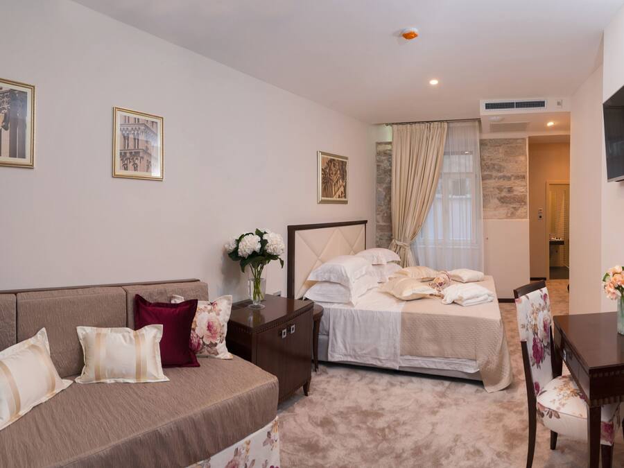 Quarto de hotel com cama, sofá, escrivaninha e televisão.
