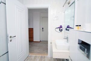 Casa de banho moderna com lavatório branco, espelho e secador de cabelo na parede.