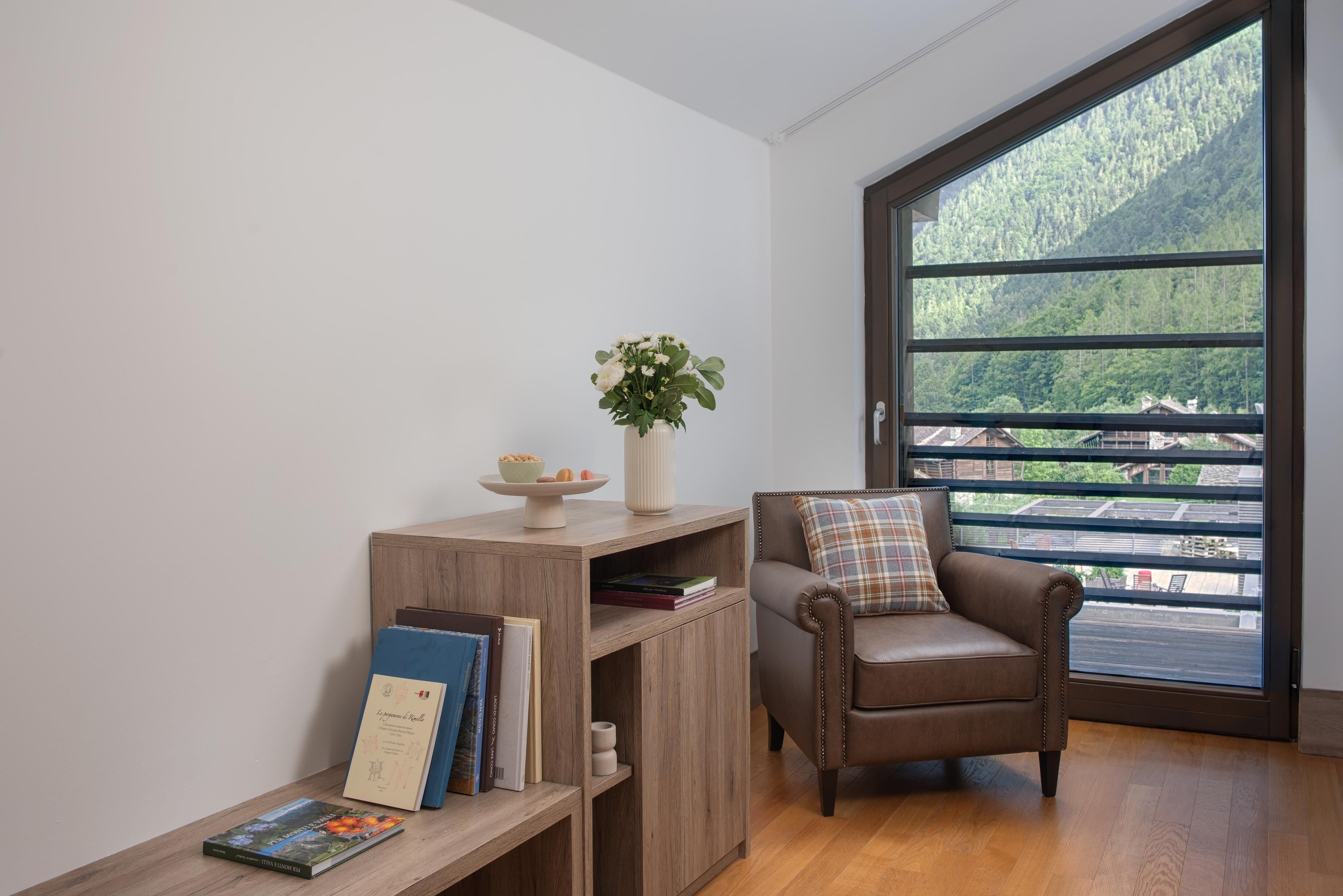 Uma sala de estar moderna com uma estante de madeira, uma poltrona de couro marrom e uma janela grande com vista para as montanhas.