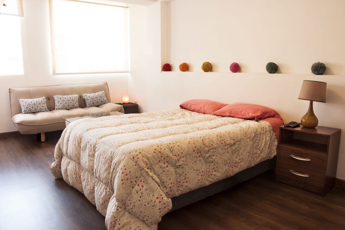 Quarto com cama, mesa de cabeceira, abajur, cômoda, janela e parede com esferas decorativas.
