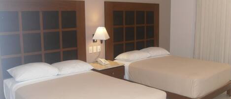 Quarto de hotel com duas camas de solteiro, mesa de cabeceira com abajur e telefone.
