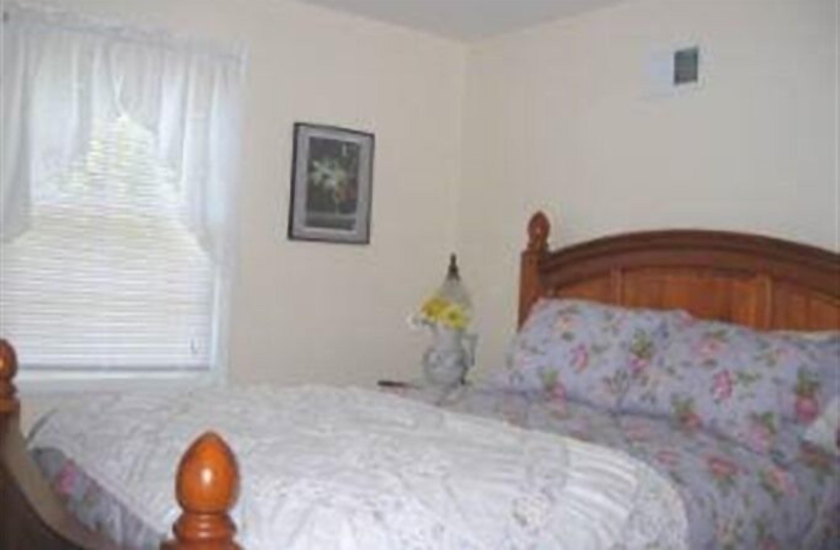Um quarto com uma cama de madeira, uma mesa de cabeceira, um quadro na parede e uma janela com cortinas.