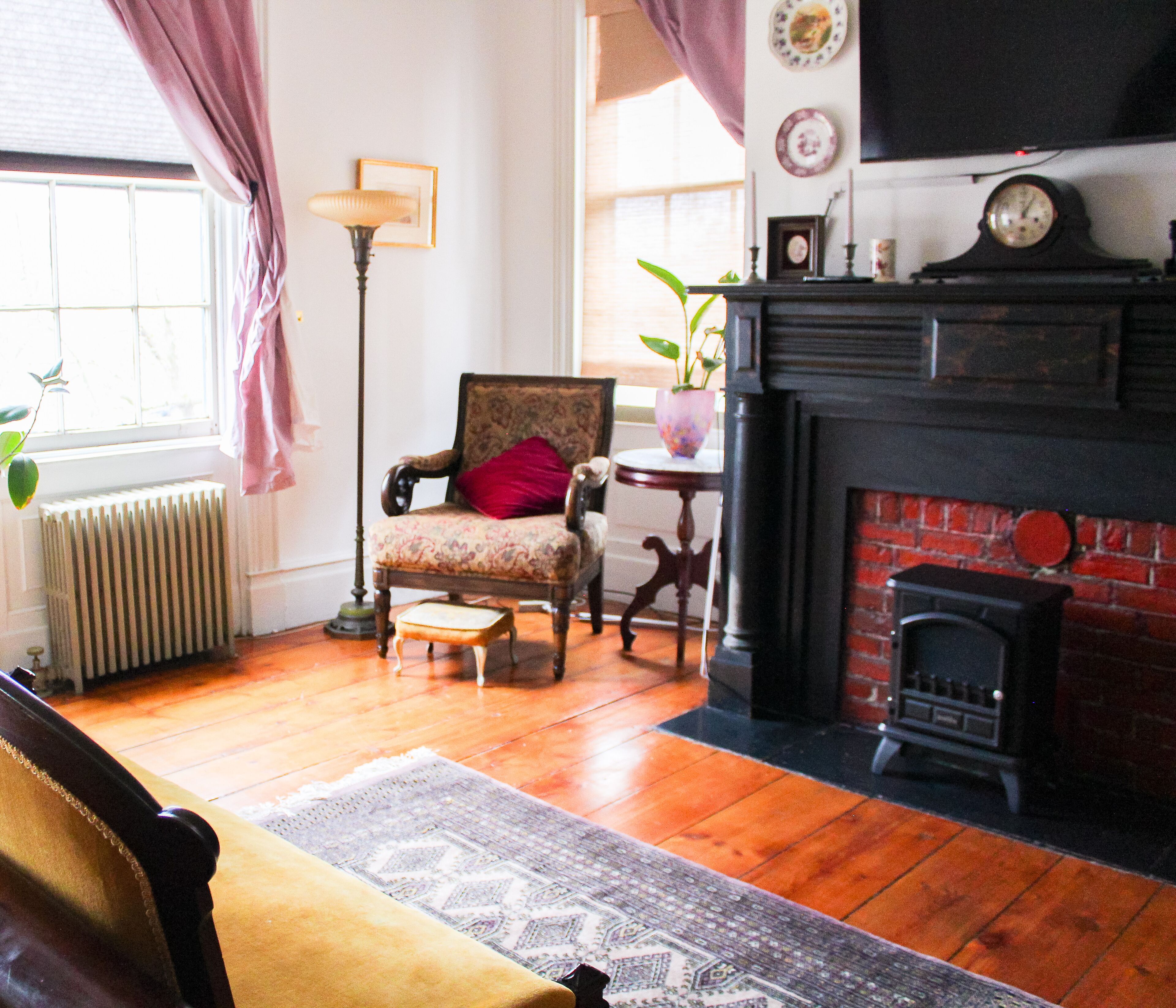 Uma sala de estar aconchegante com lareira, uma poltrona confortável, um radiador e uma janela com cortinas.