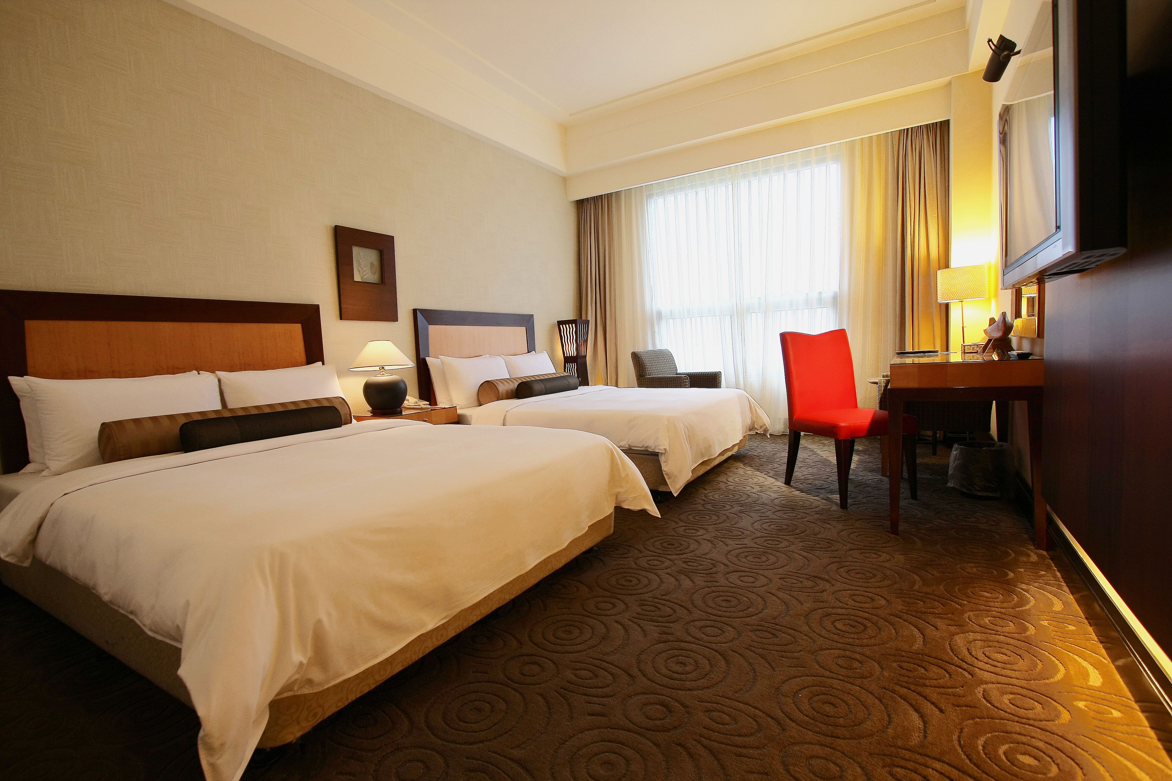 Quarto de hotel com duas camas, uma escrivaninha, uma cadeira e uma televisão.