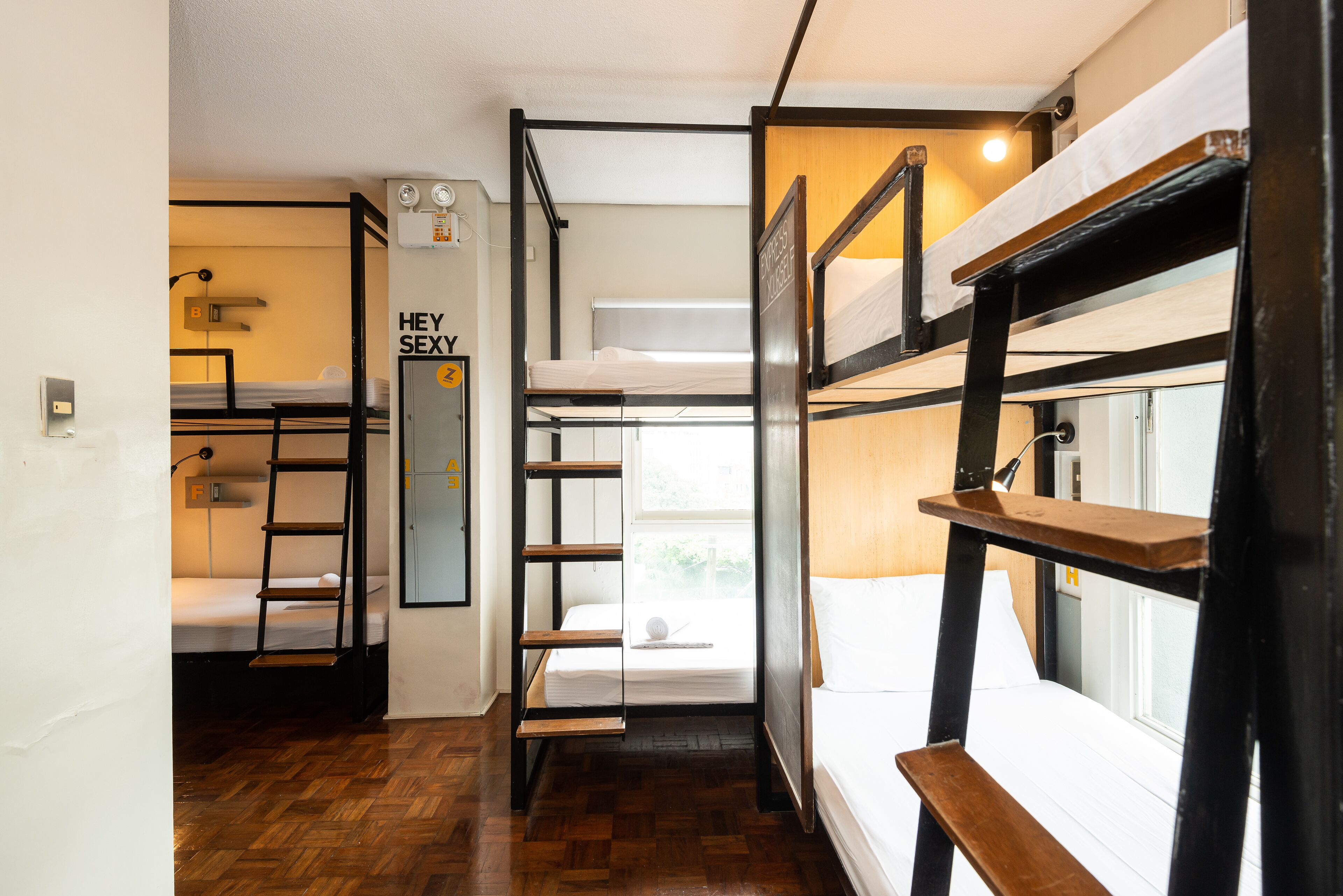 Um quarto estilo dormitório com beliches, escada, mesa e janela.