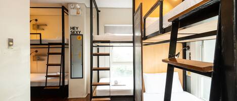 Um quarto estilo dormitório com beliches, escada, mesa e janela.