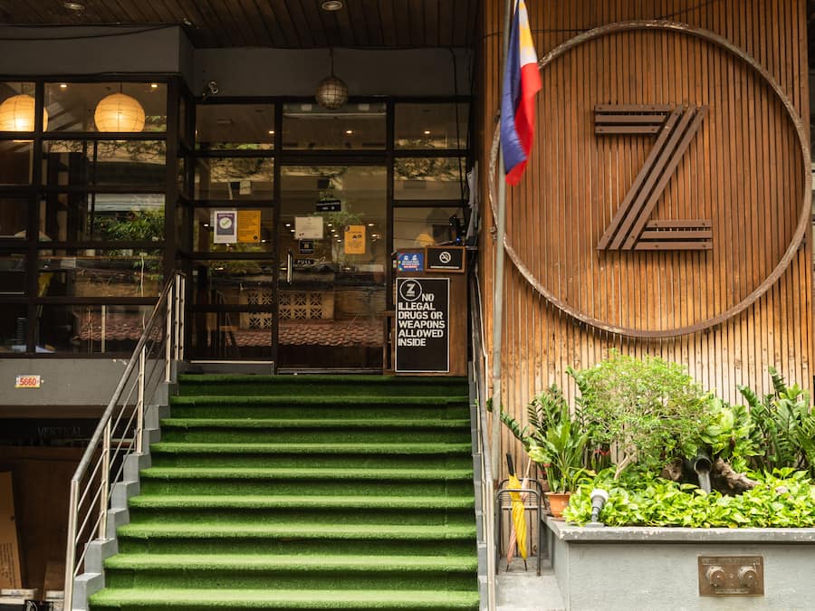 Uma escadaria com degraus verdes conduzindo a uma parede de madeira com um grande letreiro em formato de 'Z'.