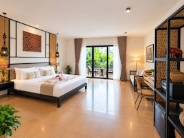Quarto de hotel com uma cama grande, uma escrivaninha, uma cadeira e uma varanda com vista para o verde.