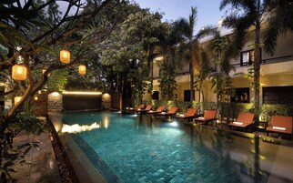 Área de piscina com espreguiçadeiras e luminárias pendentes, cercada por vegetação exuberante.