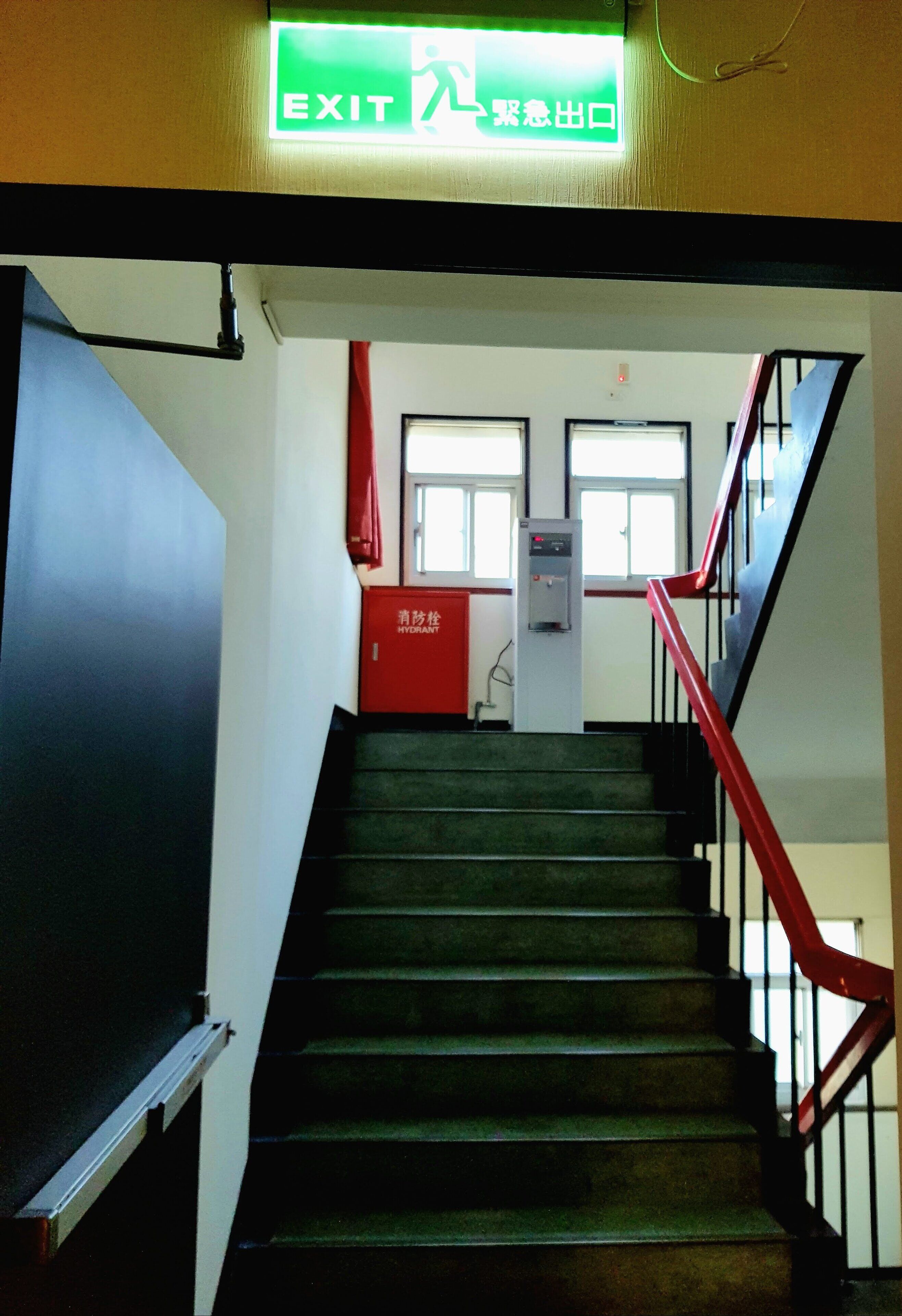 Escada com corrimão vermelho que leva a uma placa de saída.