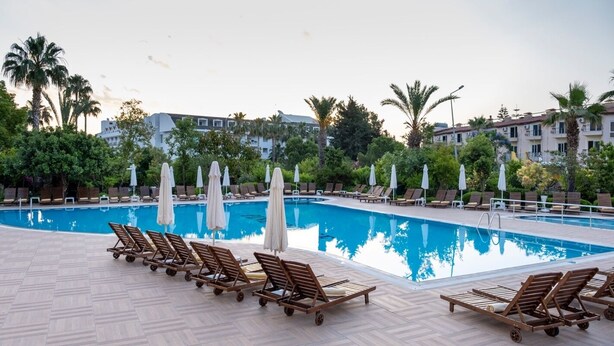 Piscina com espreguiçadeiras e guarda-sóis, cercada por vegetação e edifícios.