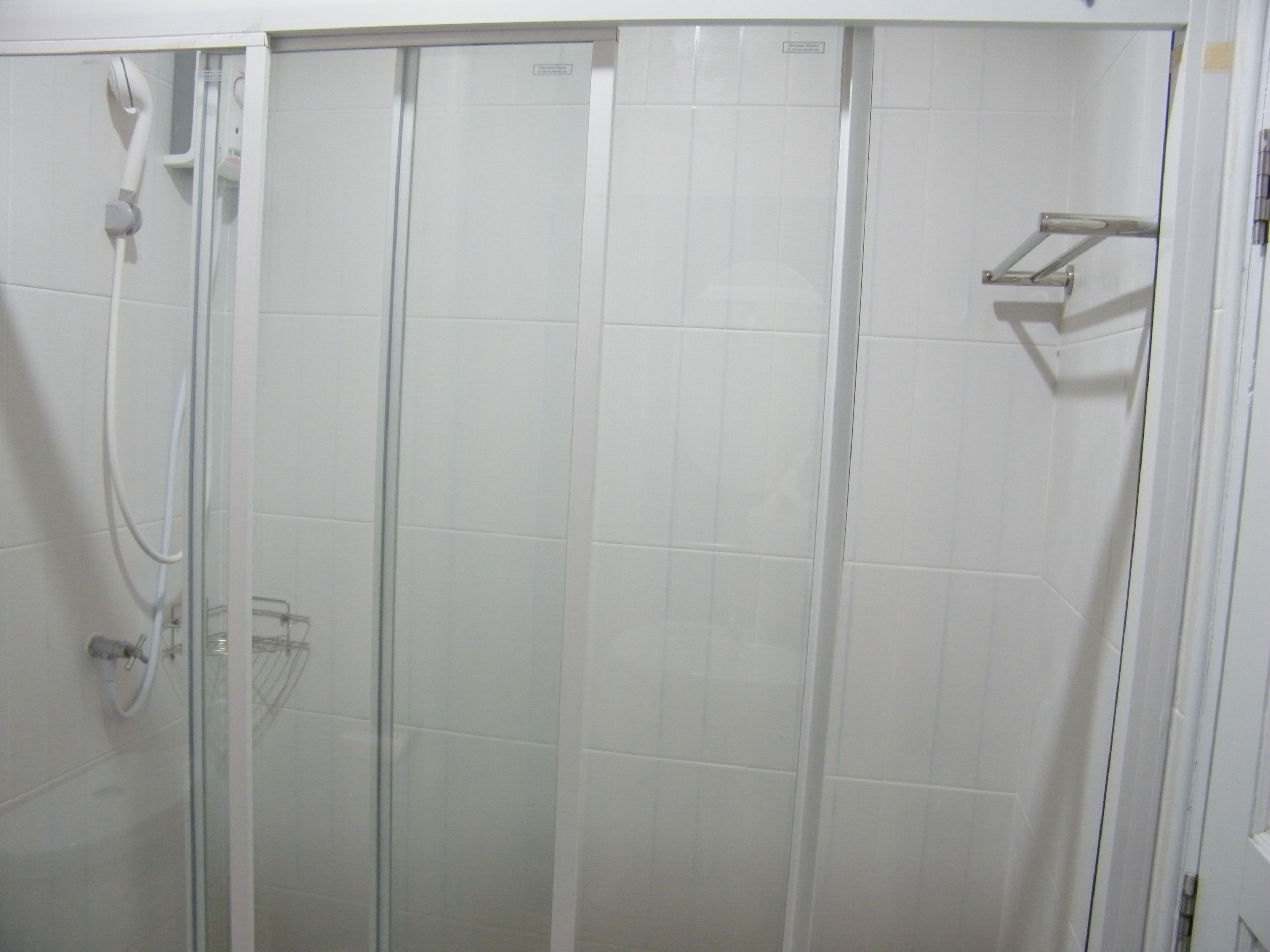 Box de vidro com parede revestida de azulejos brancos, chuveiro e porta-toalhas.