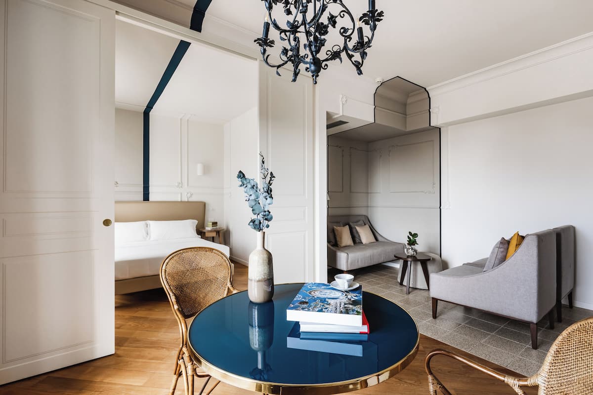 Uma sala de estar moderna com uma mesa redonda azul, um sofá e uma cadeira. Há uma estante com livros e um vaso com flores.