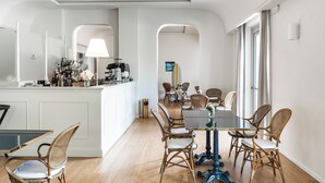 Cozinha moderna com armários brancos, uma área de jantar com cadeiras de vime e uma janela grande com cortinas.