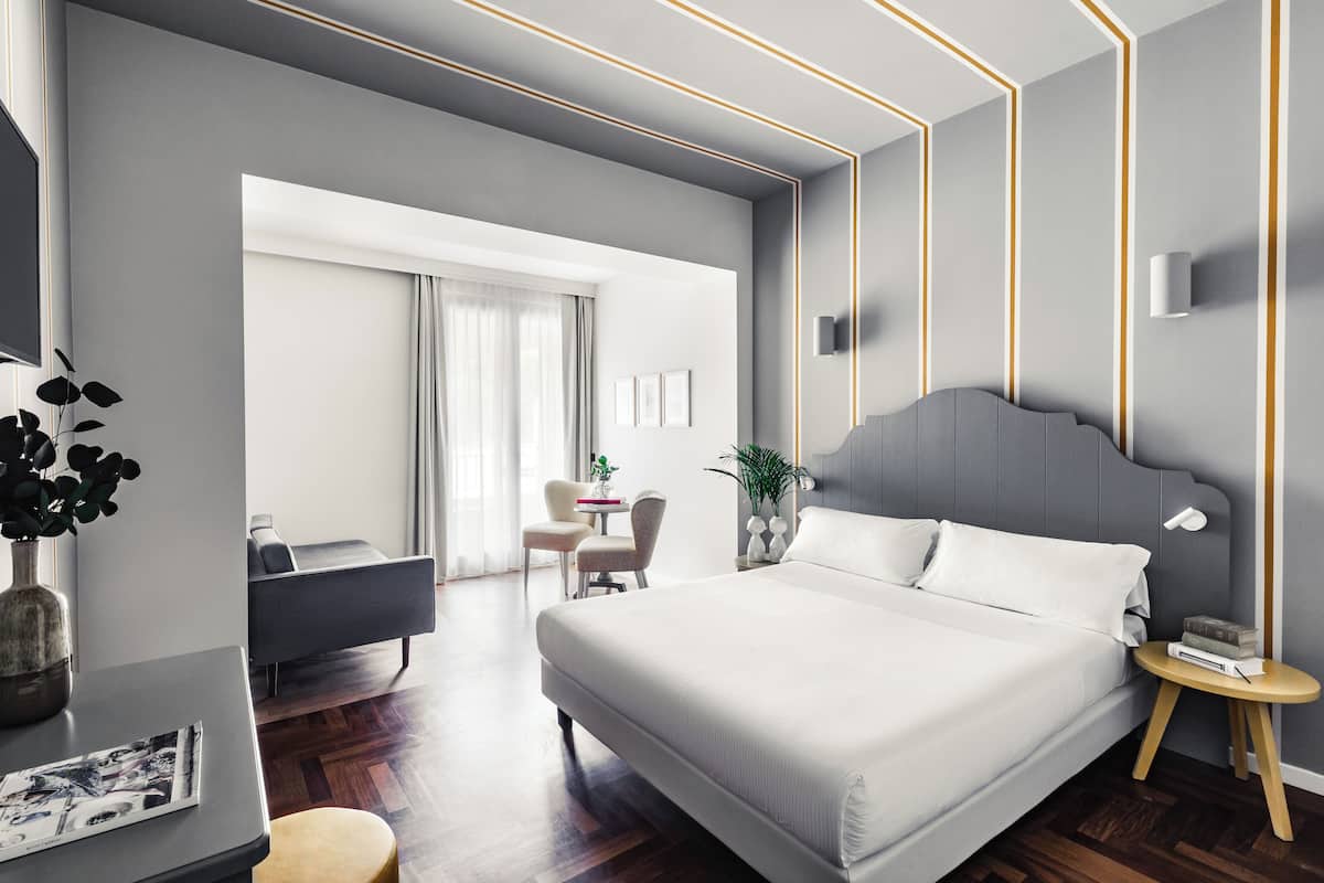Quarto de hotel moderno com uma cama grande, uma mesa de escritório e uma área de estar.