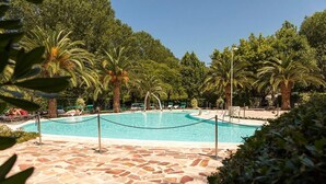 Uma área de piscina com piso de pedra, palmeiras e cadeiras de descanso.