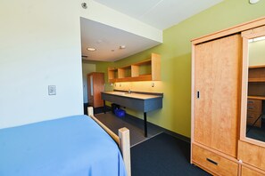 Quarto pequeno com cama, armário de madeira, pia e espelho.