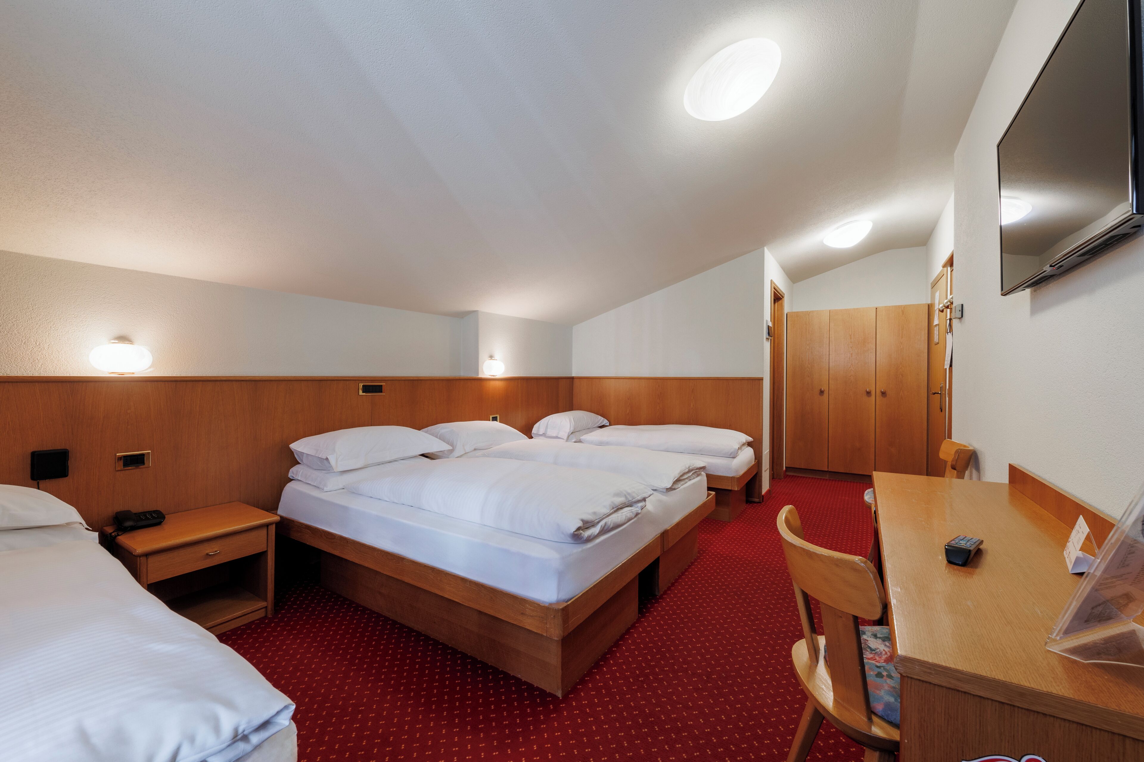 Quarto de hotel com duas camas, uma escrivaninha, uma cadeira, um guarda-roupa de madeira e uma televisão de tela plana.