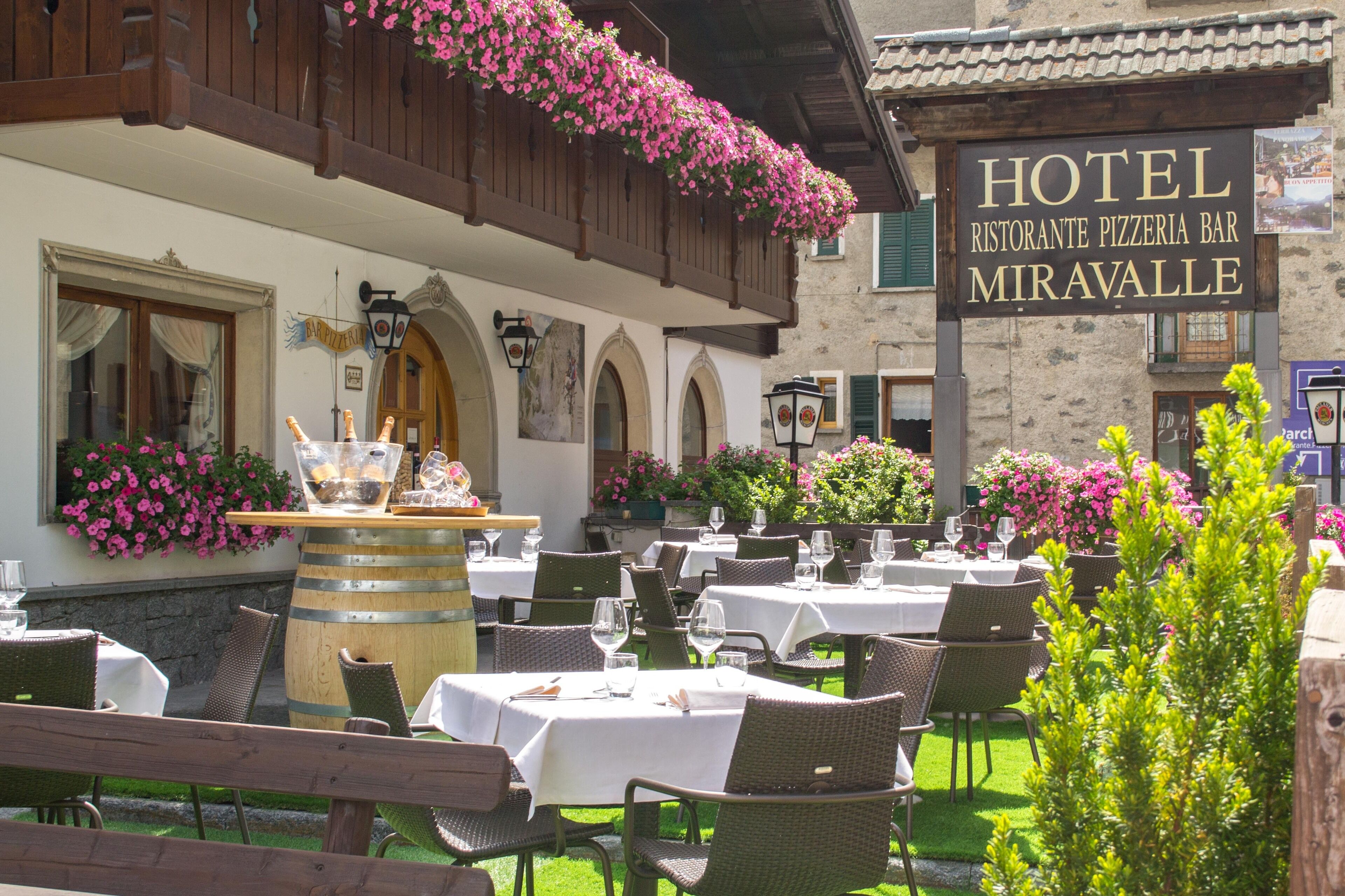 Hotel com área de refeições ao ar livre, mesas, cadeiras e placa indicando que é um restaurante e bar.